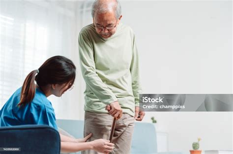 간병인과 물리 치료를하는 아시아 노인 환자 휠체어에서 일어나 집에서 보행기로 걷는 연습을 돕는 여성 간호사는 요양원에서 천천히 산책을 연습합니다 25 29세에 대한 스톡