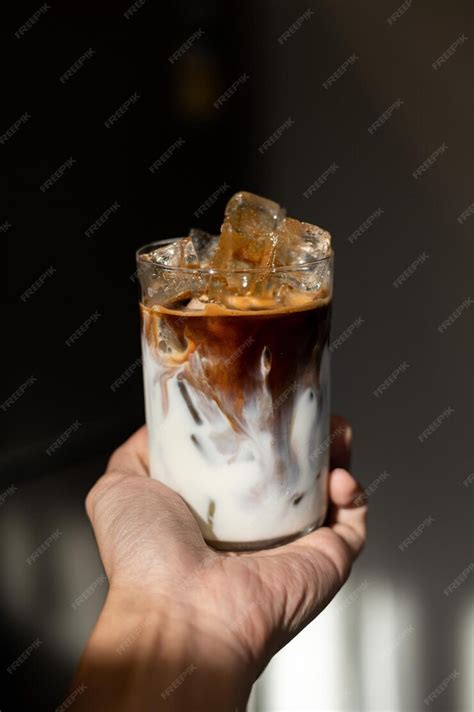 Premium Photo Iced Coffee In A Glass With Ice Cubes In Hand On Dark