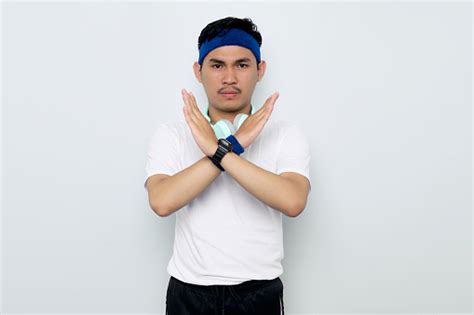 파란색 머리띠와 헤드폰이 달린 스포츠웨어 흰색 티셔츠를 입은 진지한 젊은 아시아 스포츠맨 정지 제스처 표시 거부 기호 시연 흰색 배경에 고립 된 원치 않는 것을 거부 30
