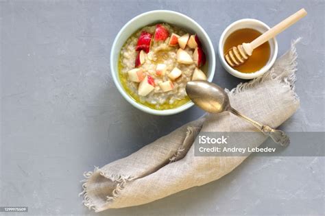 버터와 다진 빨간 사과와 함께 푸른 그릇에 담긴 오트밀 죽의 아침 식사 나무 꿀 숟가락이있는 흰색 그릇에 꿀 콘크리트 배경 여유 공간 상단 보기 건강한 식생활에 대한 스톡