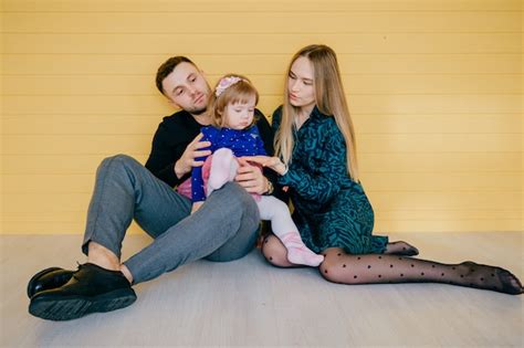 Fam Lia Jovem Alegre Com Uma Crian A Do Sexo Feminino Se Divertindo Juntos Sobre Parede Amarela