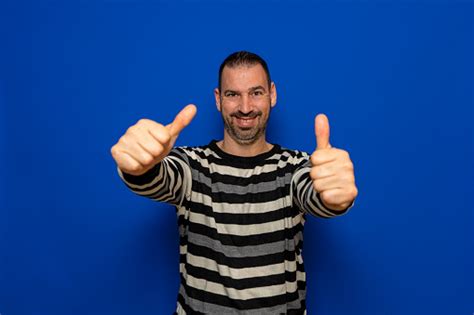 매력적인 쾌활한 핏 수염을 가진 남자는 줄무늬 풀오버에 서서 푸른 배경 위에 고립되어 엄지 손가락을 보여줍니다 개념에 대한 스톡 사진 및 기타 이미지 Istock