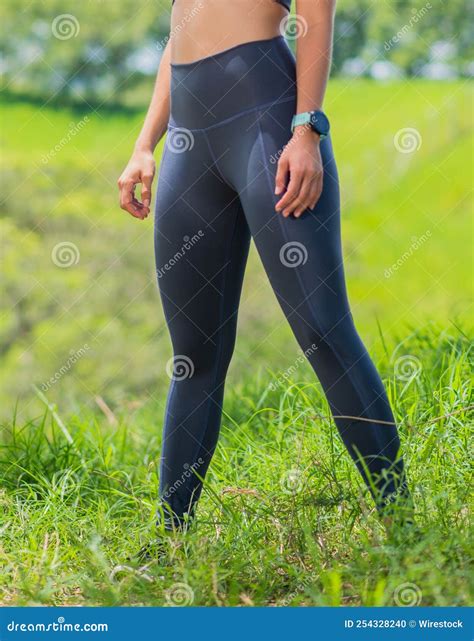 Vertical Shot Of A Fit Young Woman In Yoga Pants During Her Morning Exercise In A Sunny Green