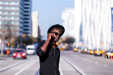 화창한 날에 휴대 전화를 사용 하는 동안 거리의 도시 풍경에 대해 서 있는 선글라스와 모자를 가진 흑인 남자의 전면 보기 거리에 대한 스톡 사진 및 기타 이미지 Istock