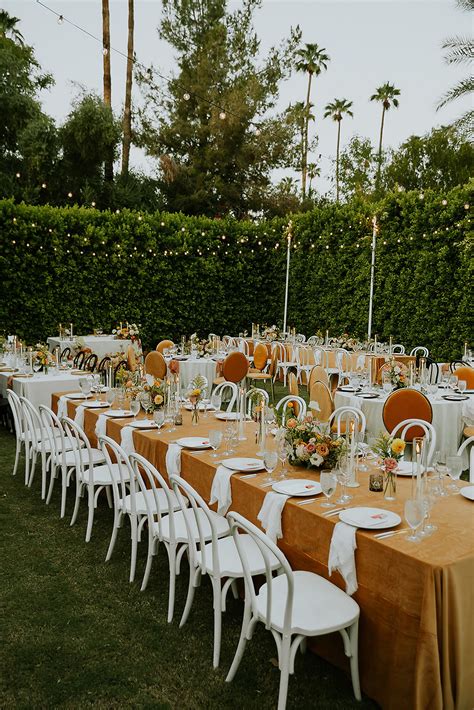 long tables with orange linens low centerpieces and candles on lawn under string lights