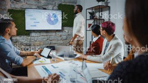 사무실 회의실 회의 흑인 수석 회사 전략가가 다민족 전문 기업인의 다양한 팀에 Tv 프레젠테이션을하고 마케팅 전략 데이터 분석을 설명합니다 단체에 대한 스톡 사진 및 기타