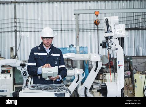 Engineer Controlling Robot Arm At Factory Checking The Operation Of