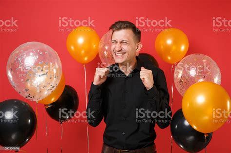 행복 한 미소 블랙 클래식 셔츠 빨간색 배경 공기 풍선에 우승자 몸짓을 하 고 젊은 남자 세인트 발렌타인 국제 여성의 날 해피 뉴가 어 생일 이랑 휴일 파티 개념 12월