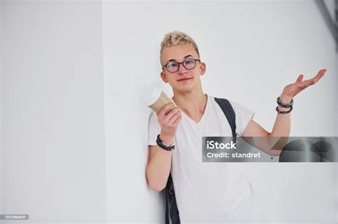 캐주얼 한 옷을 입고 배낭을 입은 학생이 음료 한 잔으로 흰색 벽에 실내에 서 있습니다 20 24세에 대한 스톡 사진 및 기타 이미지 20 24세 개인 장식품 남성