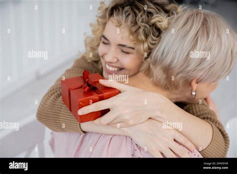 Overjoyed Woman With Closed Eyes Holding Gift Box And Embracing Middle