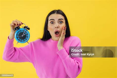 노란색 배경의 스튜디오에서 알람 시계를 들고 충격을 표현하는 예쁜 여자 시간을 놓치고 중요한 회의에 늦어서 스트레스를 받습니다 25 29세에 대한 스톡 사진 및 기타 이미지