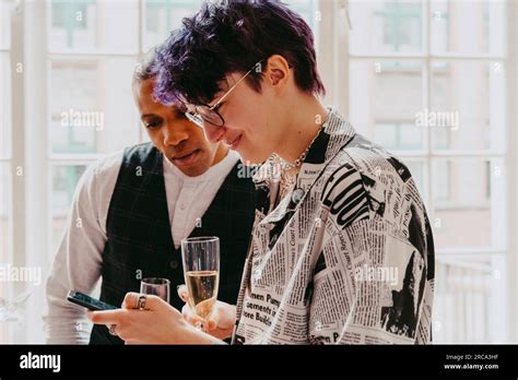 Smiling Non Binary Person Sharing Smart Phone With Male Colleague During Event At Convention