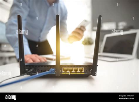 Wireless Router With Three Antennas And Cable Connected Man Using Smartphone In Background