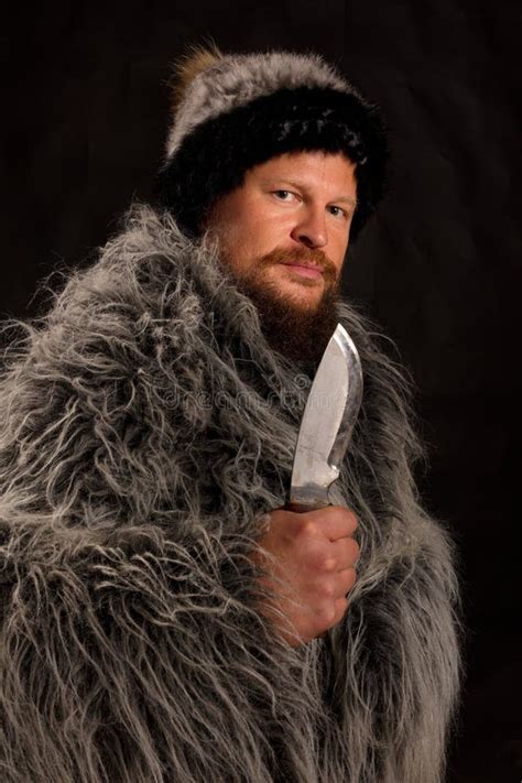 Bearded Hunter Dressed In A Fur Mantle And Fur Hat With Knife Stock