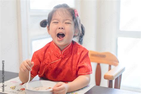 Small Asian Girl In Chinese Traditional Dress Eating Vegetables And Sausage In Restaurant And