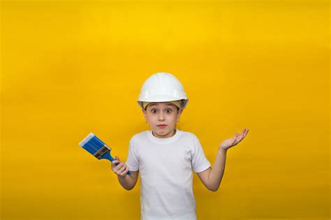 건설 흰색 헬멧에 놀란 어린 소녀가 노란색 배경에 페인트 브러시를 들고있다 Diy에 대한 스톡 사진 및 기타 이미지 Diy