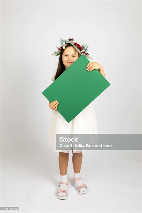 크리스마스 화환과 흰색 배경에 고립 된 녹색 빈 배너를 손에 들고 흰색 축제 드레스에 귀여운 소녀의 전체 길이 초상화 2021년에 대한 스톡 사진 및 기타 이미지 Istock