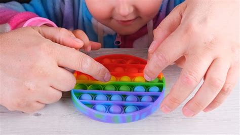 귀여운 어린 소녀는 팝 그 감각 장난감 원 형태로 아빠와 함께 재생합니다 작은 여성은 흰색 배경에 화려한 무지개 Squishy 부드러운 실리콘 거품을 누릅니다 스트레스와