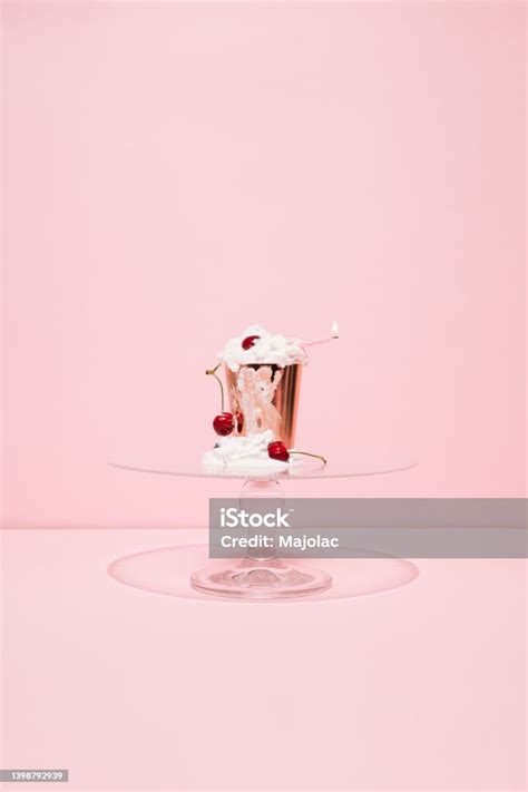 유리 케이크에 녹는 휘핑 크림 체리 및 불타는 양초가있는 황금 종이 컵은 분홍색 배경에 서 있습니다 여름 컵케이크 최소한의 개념 개념에 대한 스톡 사진 및 기타 이미지