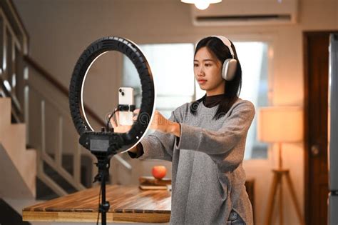 Teenage Woman In Headphone Setting Up Her Smartphone On A Ring Light For Content Creation Stock