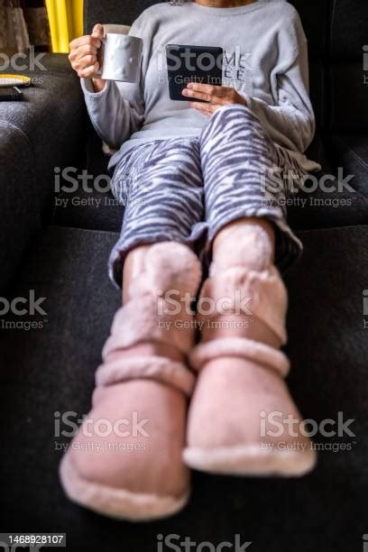 잠옷을 입은 성인 여성은 전자책 장치에서 책을 읽고 집 거실 소파에서 커피 한 잔을 홀짝입니다 50 54세에 대한 스톡 사진 및 기타 이미지 Istock