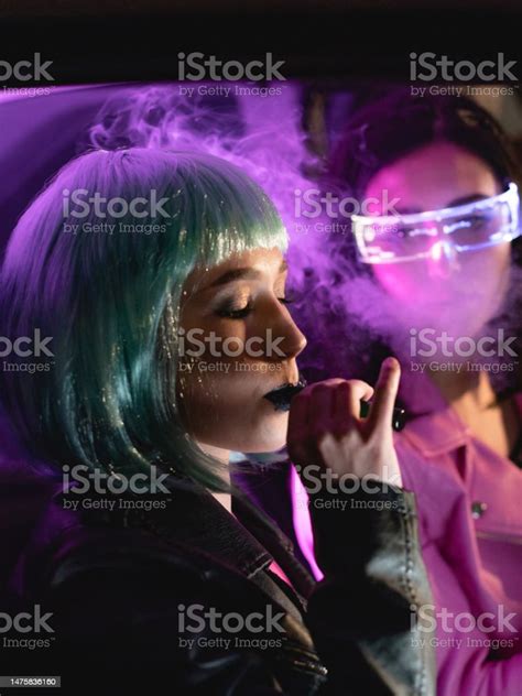 Female Portrait Of Two Women Who Wear Futuristic Glasses And Using Vape