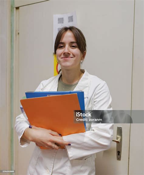 실험복을 입은 여대생이 손에 폴더를 들고 문 옆에 서 있습니다 18 19세에 대한 스톡 사진 및 기타 이미지 18 19세 Educational Institutions