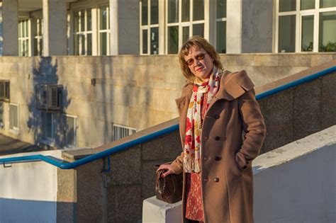 석양에 이른 봄에 사무실 건물의 계단에 가방에 서 있는 세련 된 코트를 입고 매력적인 중 년 여성 스트리트 시티 초상화 패션 도시 복장 가방에 대한 스톡 사진 및 기타