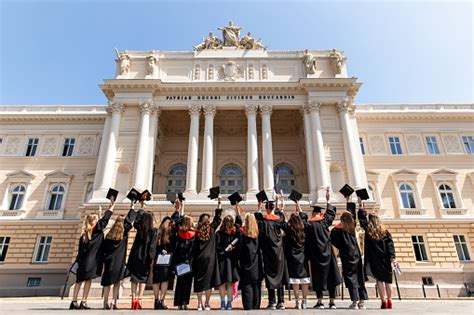 가운을 입은 졸업생 그룹은 교육에 대한 명예와 존중의 상징으로 대학 건물을 배경으로 학업 모자를 올렸습니다 졸업식에 대한 스톡 사진 및 기타 이미지 Istock