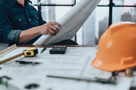 사무실 책상과 계산기 삼각형 눈금자 안전 안경 나침반 블루프린트의 버니어 캘리퍼에서 도면 검사를 수행하는 엔지니어링 엔지니어 건축가 산업 및 공장 개념 개발에 대한 스톡