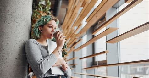 캐주얼 옷을 입은 대체 소녀와 녹색 머리가 낮에 실내에 서서 음료수 한 잔을 손에 들고 있습니다 사진 Unsplash의 우크라이나 이미지