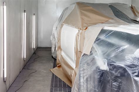 대형 흰색 차는 밝은 조명이 있는 차량의 차체 수리를 위한 워크샵에서 사고 후 페인팅 및 수리 중 스플래시를 방지 하기 위해 종이 및 접착 테이프로 완전히 덮여 있습니다