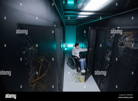 Wide Angle Portrait Of Disabled Woman In Wheelchair Working With Supercomputer Network In Server