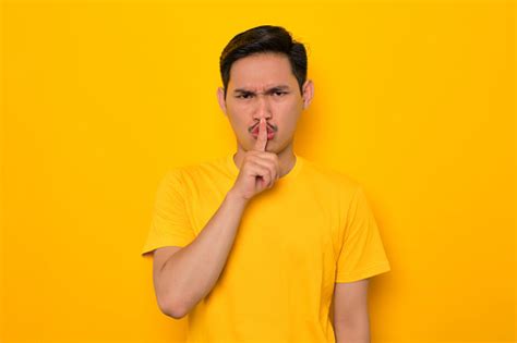 Shh 제스처를 보여주는 캐주얼 티셔츠를 입은 매력적인 젊은 아시아 남자는 노란색 배경에 고립 된 입술에 손가락을 누릅니다 사람들 라이프 스타일 개념 30 34세에 대한