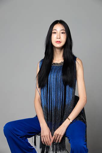 긴 검은 직선 머리를 가진 아시아 트랜스젠더 여성 카메라를보십시오 여성은 앉아서 블루 패션 관능적 인 섹시한 드레스 회색 배경