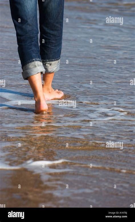The Bare Feet Of A Man Wearing Jeans With Rolled Up Legs On The Beach