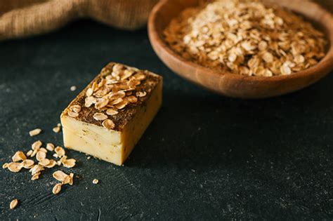 귀리 플레이크가 담긴 나무 숟가락 귀리를 얹은 소박한 비누 바 어두운 질감의 배경에 플레이크가 가득 담긴 나무 그릇은 천연 및 유기농 제품을 강조합니다 귀리에 대한 스톡