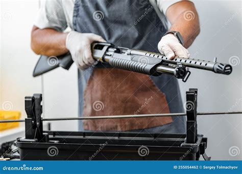 Close Up Of Young Man In Apron Disassembling A Gun Above The Table