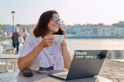 노트북과 스마트 폰을 사용하여 커피 한 잔을 들고 야외 카페에 앉아있는 비즈니스 여성 40 49세에 대한 스톡 사진 및 기타 이미지 40 49세 45 49세