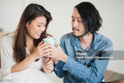 젊은 부부는 흰색 침대에 앉아 아시아 남자와 여자를 사랑하고 침대 방에 물 한 잔을 개최합니다 남자와 여자 기쁜 미소와 돌봐 행복 벌채 집에서 커플 사랑의 생활 2명에 대한