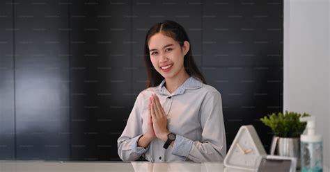 리셉션 데스크에 앉아 손을 드는 젊은 아시아 여성 접수 원은 호텔 방문객을 환영하기 위해 경의를 표합니다 사진 Unsplash의 사업 이미지