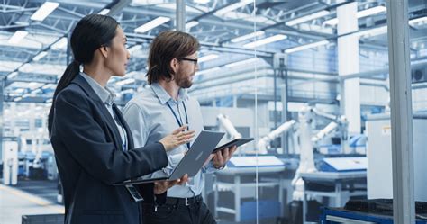 쾌활한 엔지니어와 행복한 아시아 과학자가 노트북과 태블릿 컴퓨터를 사용하여 공장 시설에서 다양한 산업을 위한 최신 전자 부품을 생산하는 로봇과 이야기하는 모습 제조에 대한