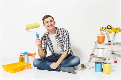 페인트 롤러 악기 재건축 아파트 방 바닥에 앉아 캐주얼 옷에서 남자 흰색 배경에 고립 벽지 액세서리를 붙이기 그림 도구 수리 가정 개념입니다 개선에 대한 스톡 사진 및 기타