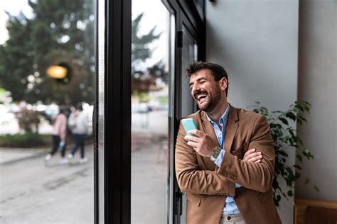 스마트 폰을 사용하는 사려 깊은 사업가가 사무실에 서서 대도시의 창밖을 내다보고 있습니다 카리스마 넘치는 디지털 기업가 계획 전자 상거래 스타트업을 위한 투자 전략 사업