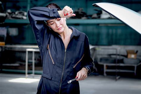 제복을 입은 아름다운 여성 자동차 정비사는 차고에서 엔진 차량으로 작업하는 동안 피곤함을 느낀다 지친 기술자 여성이 자동차 자동차 수리 서비스 가게에서 고객 차를 수리하고