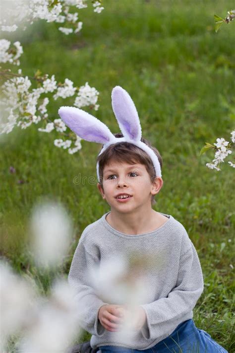 Cute Smiling Boy With Bunny Ears Siting On Green Lawn Against