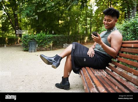 Full Body Happy Asian Non Binary Person In Feminine Clothes Smiling And Watching Video On