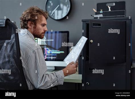 Side View Portrait Of Bearded It Programmer Reading Document At