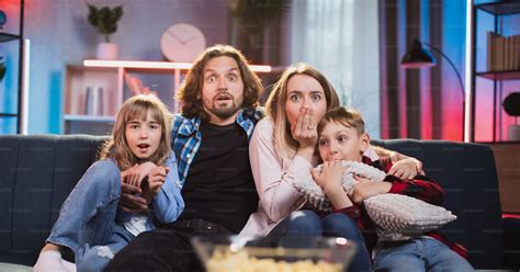 집에서 저녁 시간에 Tv에서 공포 숨막히는 영화를 보는 작은 아들과 딸을 둔 무서워하거나 놀란 젊은 부모 실제 인간의 감정 가족 여가 개념입니다 사진