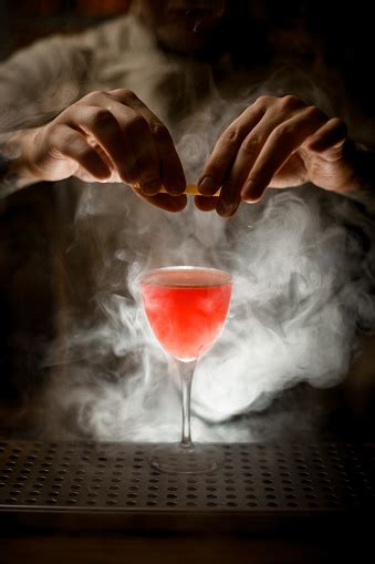 레몬 껍질을 들고 있는 바텐더의 클로즈업 보기와 스모키 바에서 칵테일을 곁들인 유리에 뿌려보냅니다 감귤류 과일에 대한 스톡 사진